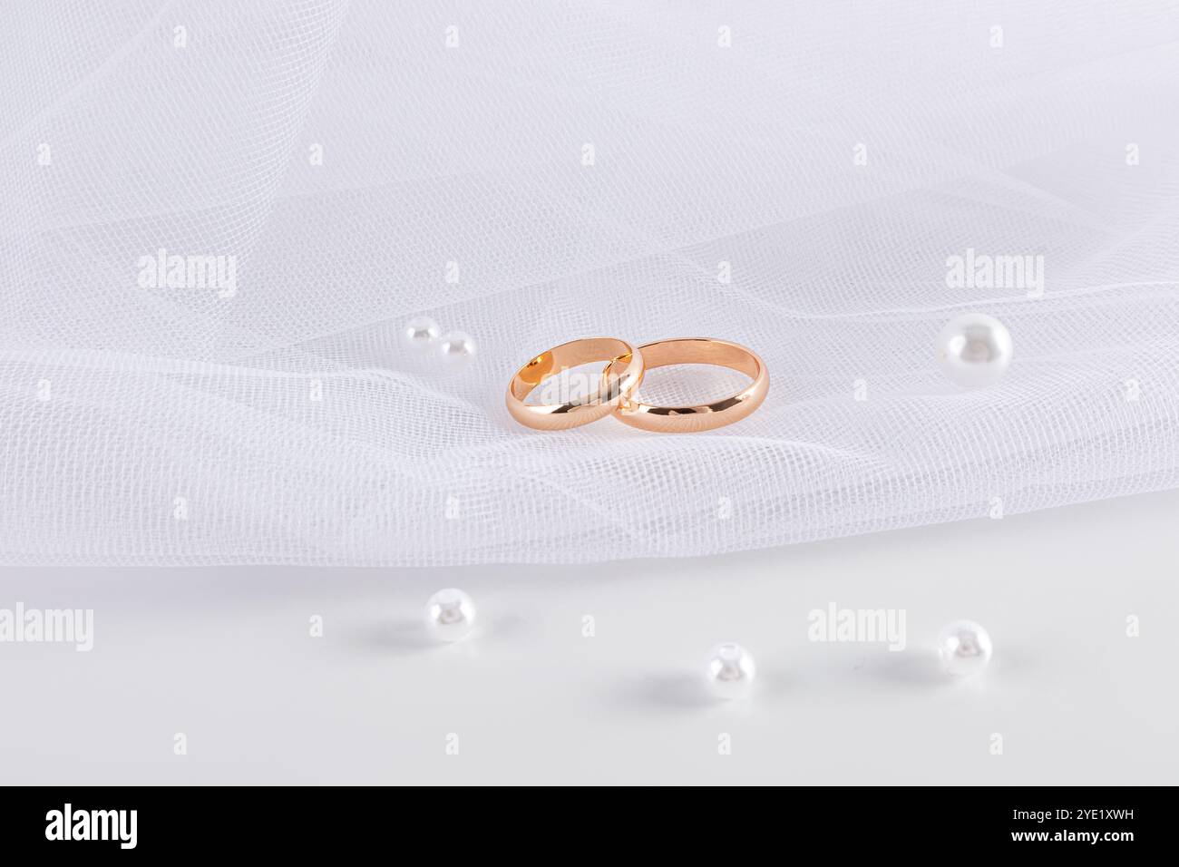Two classic gold wedding rings lie on a white bridal veil with pearls ...
