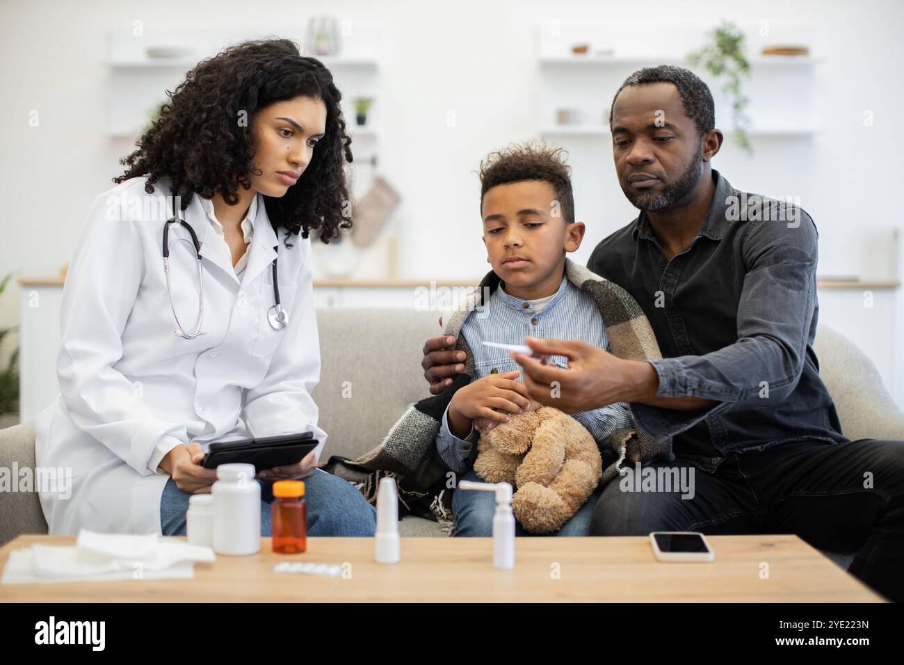 African female doctor assessing child's temperature at home visit Stock ...
