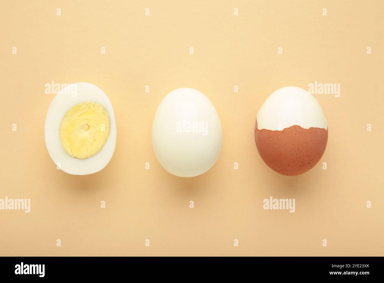 Whole white egg and halved boiled egg with yolk on beige background ...