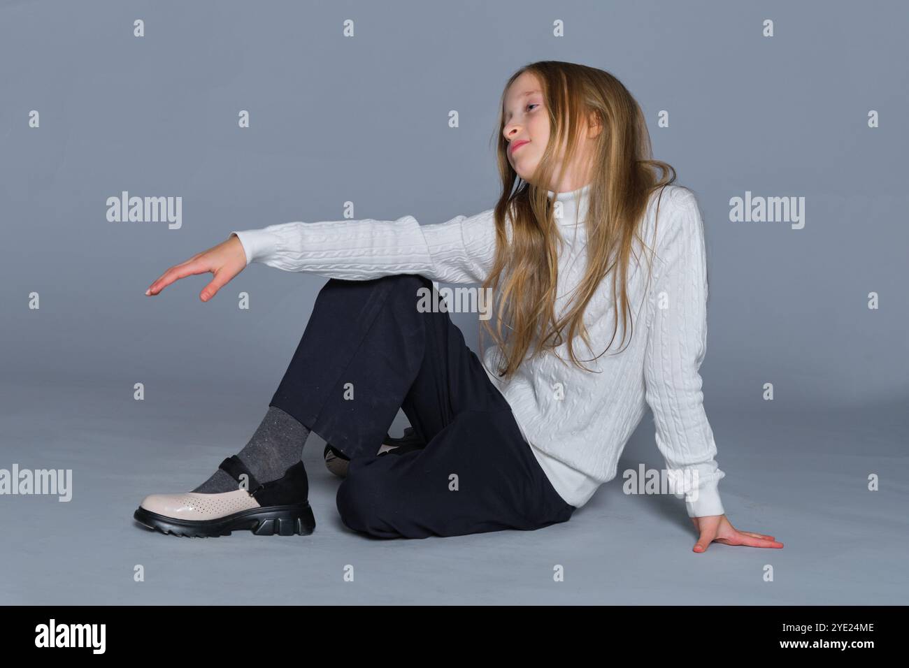 A young girl sits on the floor, stretching one arm out in a relaxed ...