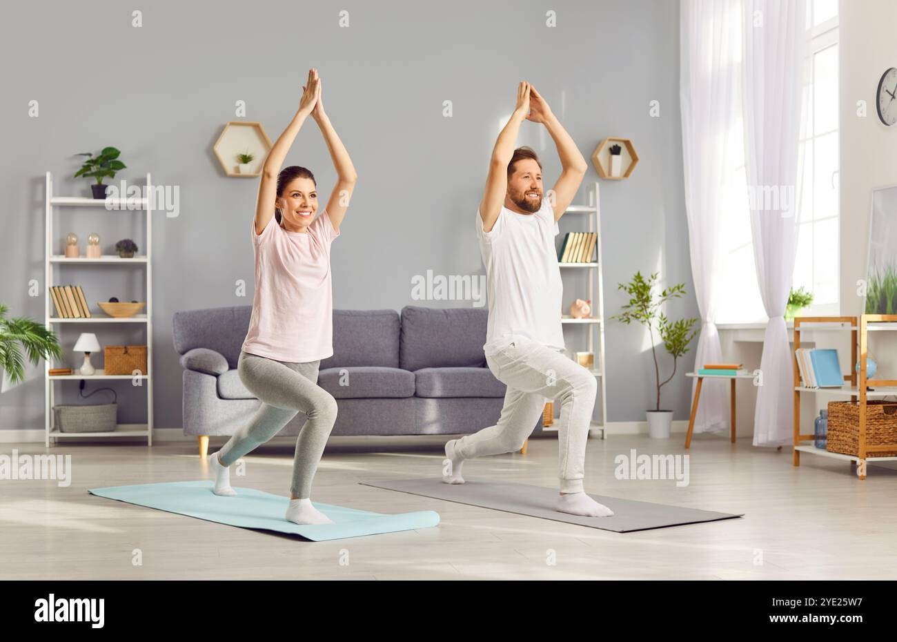 Happy young adults couple standing together in high lunge yoga pose in ...
