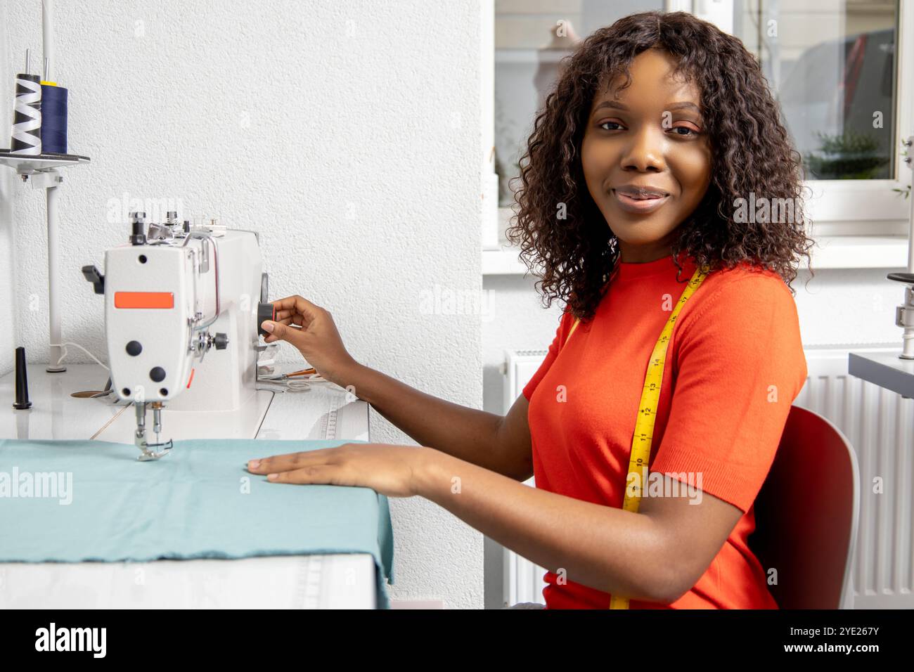 African american dressmaker sitting at the sewing machine and looking ...