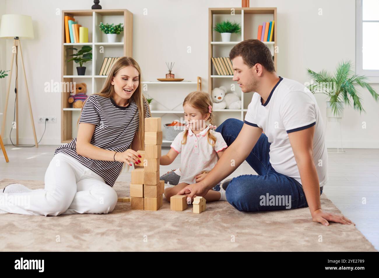 Happy parents playing educational game with daughter, building tower ...
