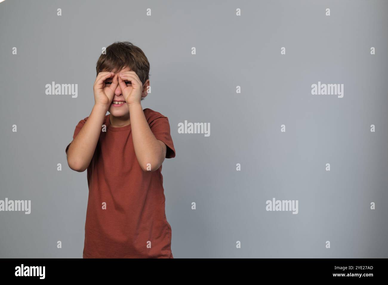 A young boy mimics binoculars with his hands, smiling and peering ...
