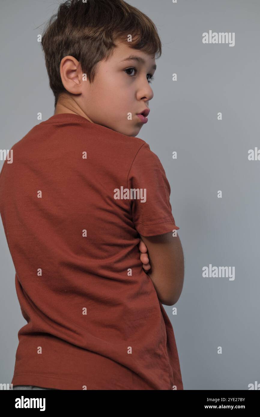 A young boy, arms crossed, looks away with a focused expression. This ...