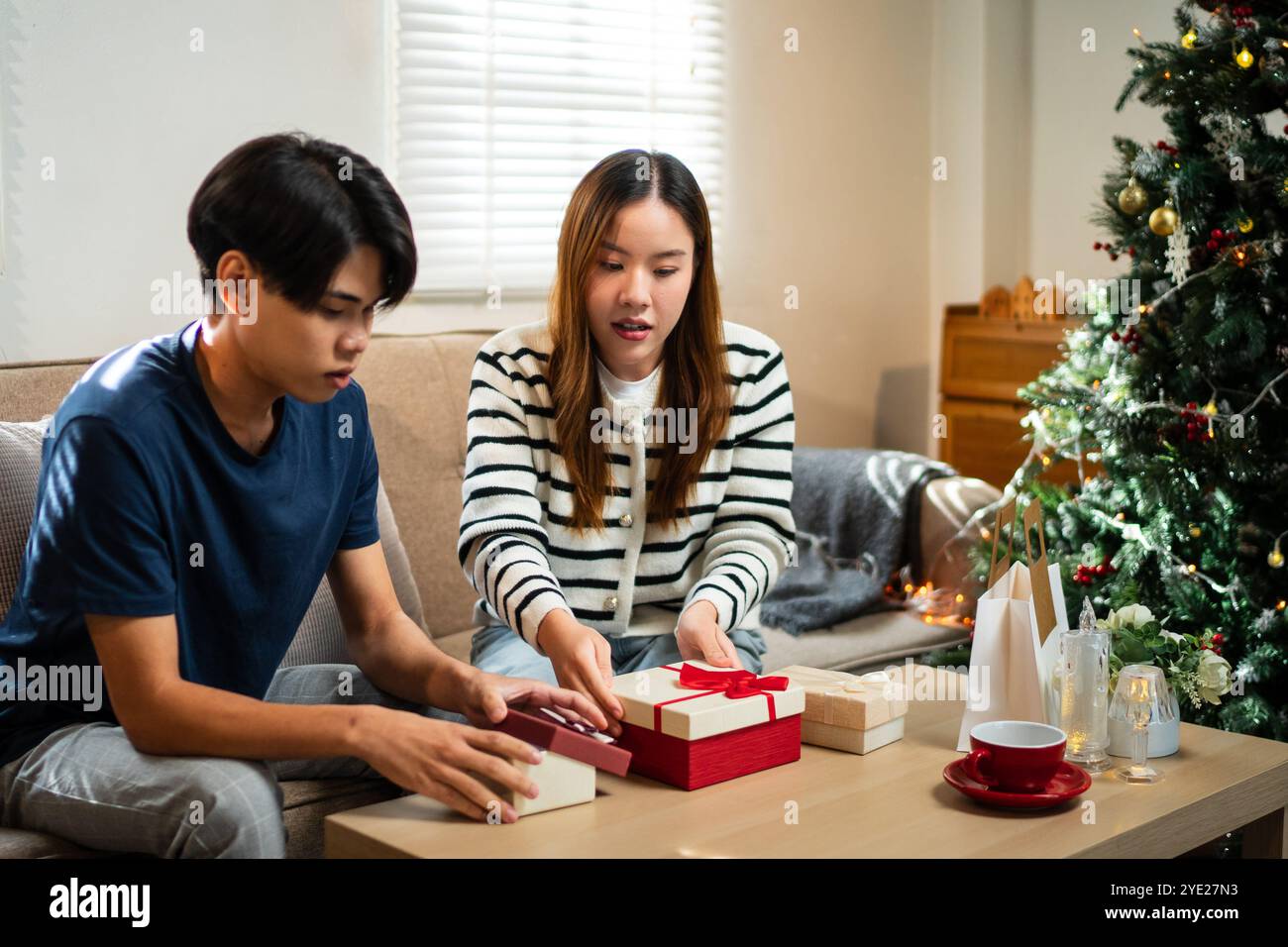 A young man and woman are sitting near a Christmas tree, sharing a ...