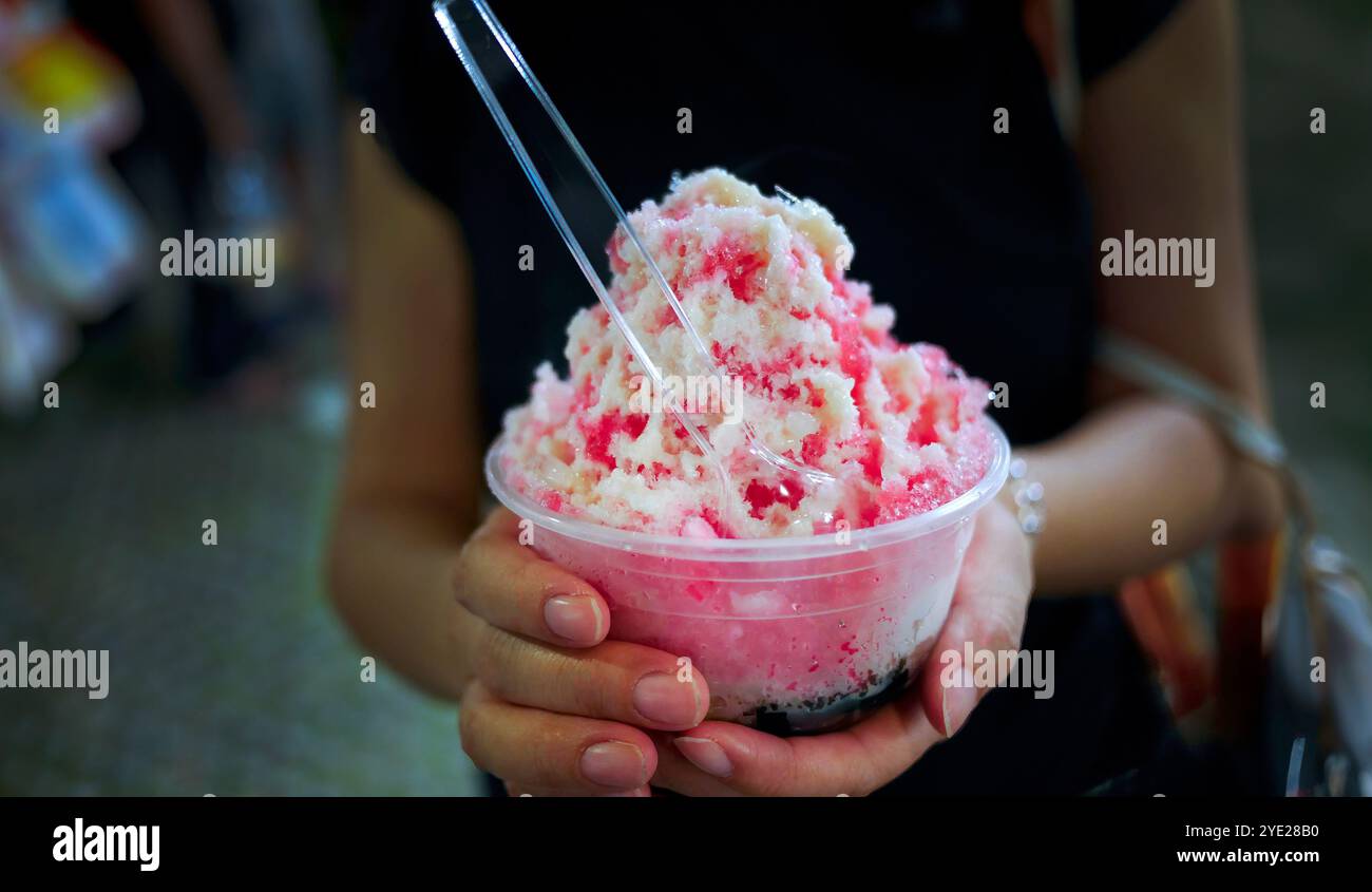 Female hands holding a plastic bowl of Red syrup shaved ice dressing ...