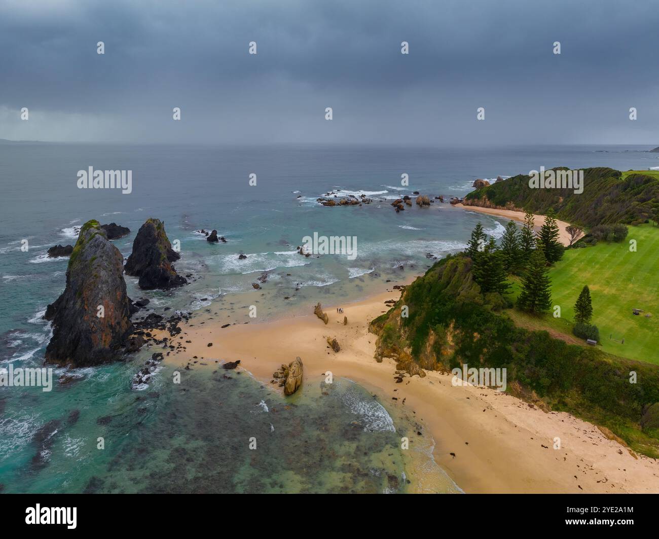 Aerial view of jagged rock formations off a coastal beach with rain ...