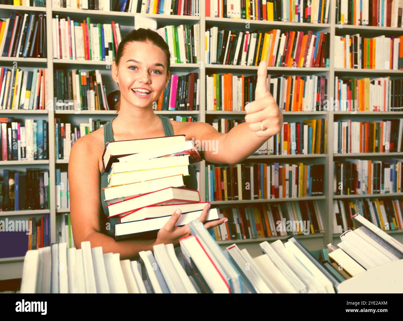 Girl holding stack of books shows thump up Stock Photo - Alamy