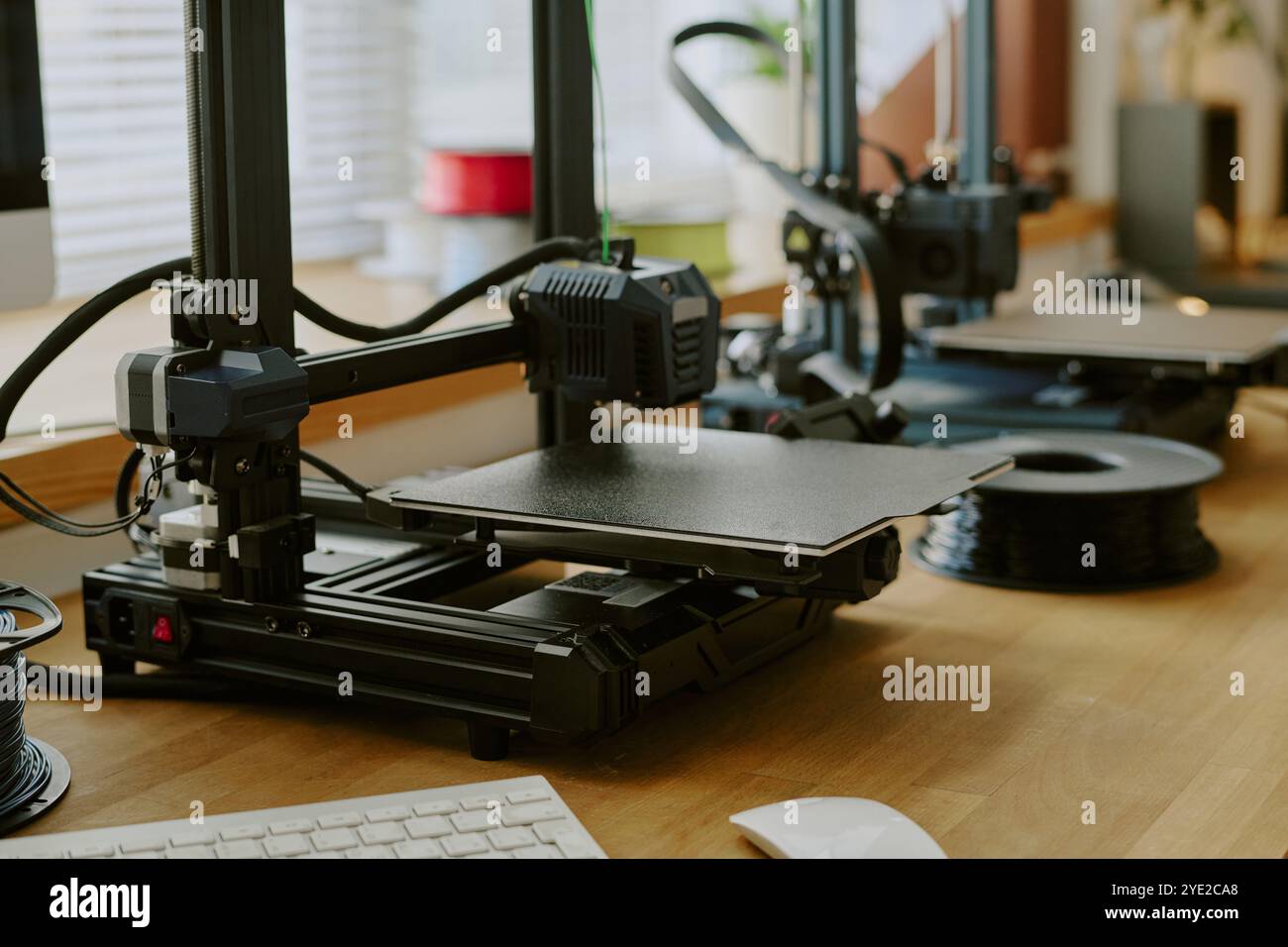 Several advanced 3D printers arranged on wooden desk in brightly lit ...