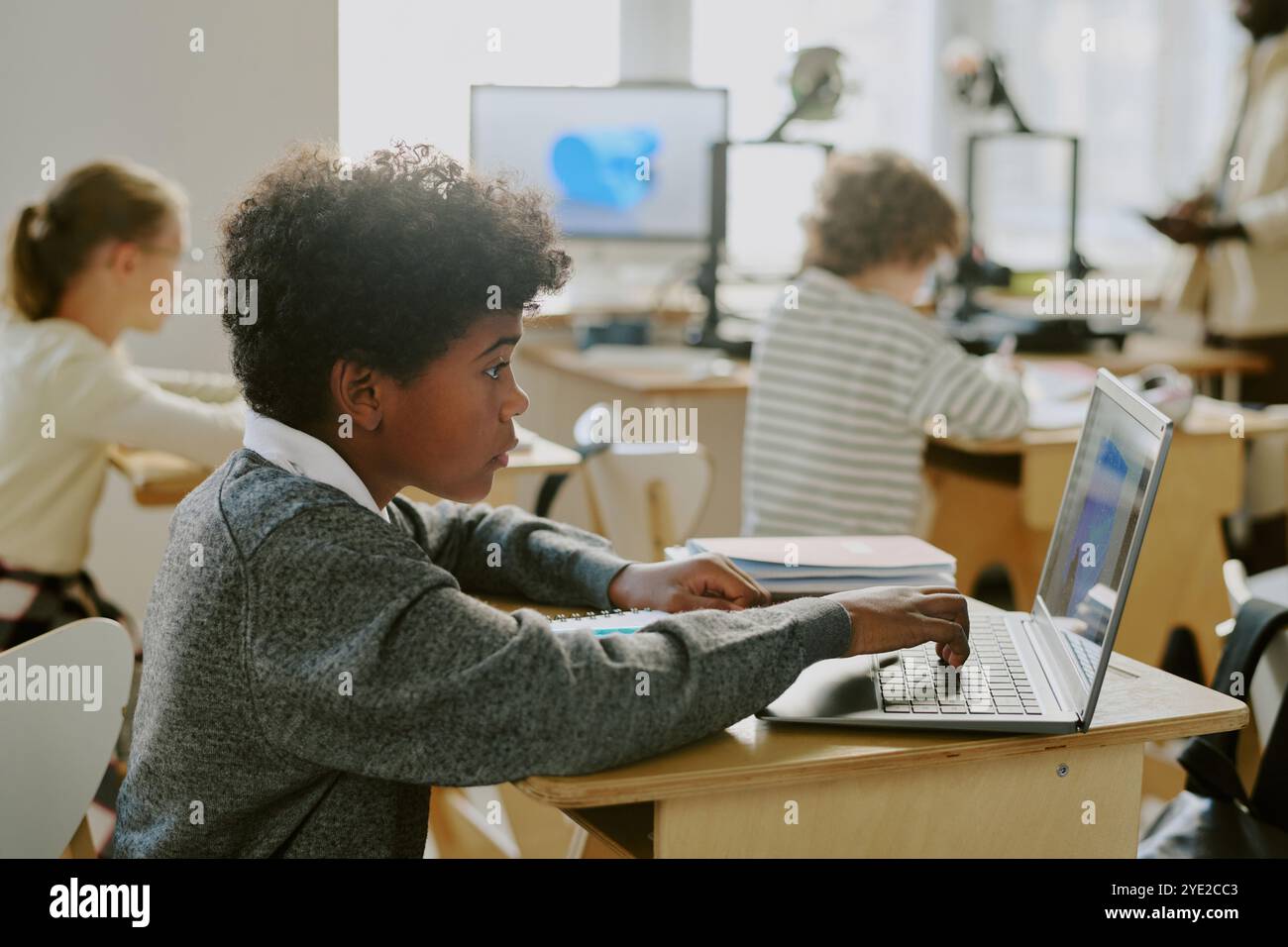Focused student studying at classroom desk during lesson, using laptop ...