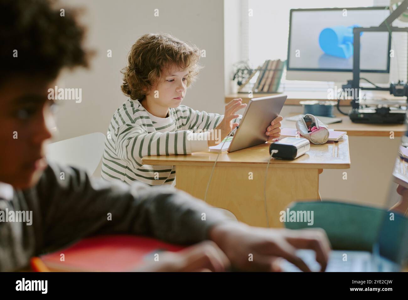 Two boys engaged with educational devices at classroom desks learning ...