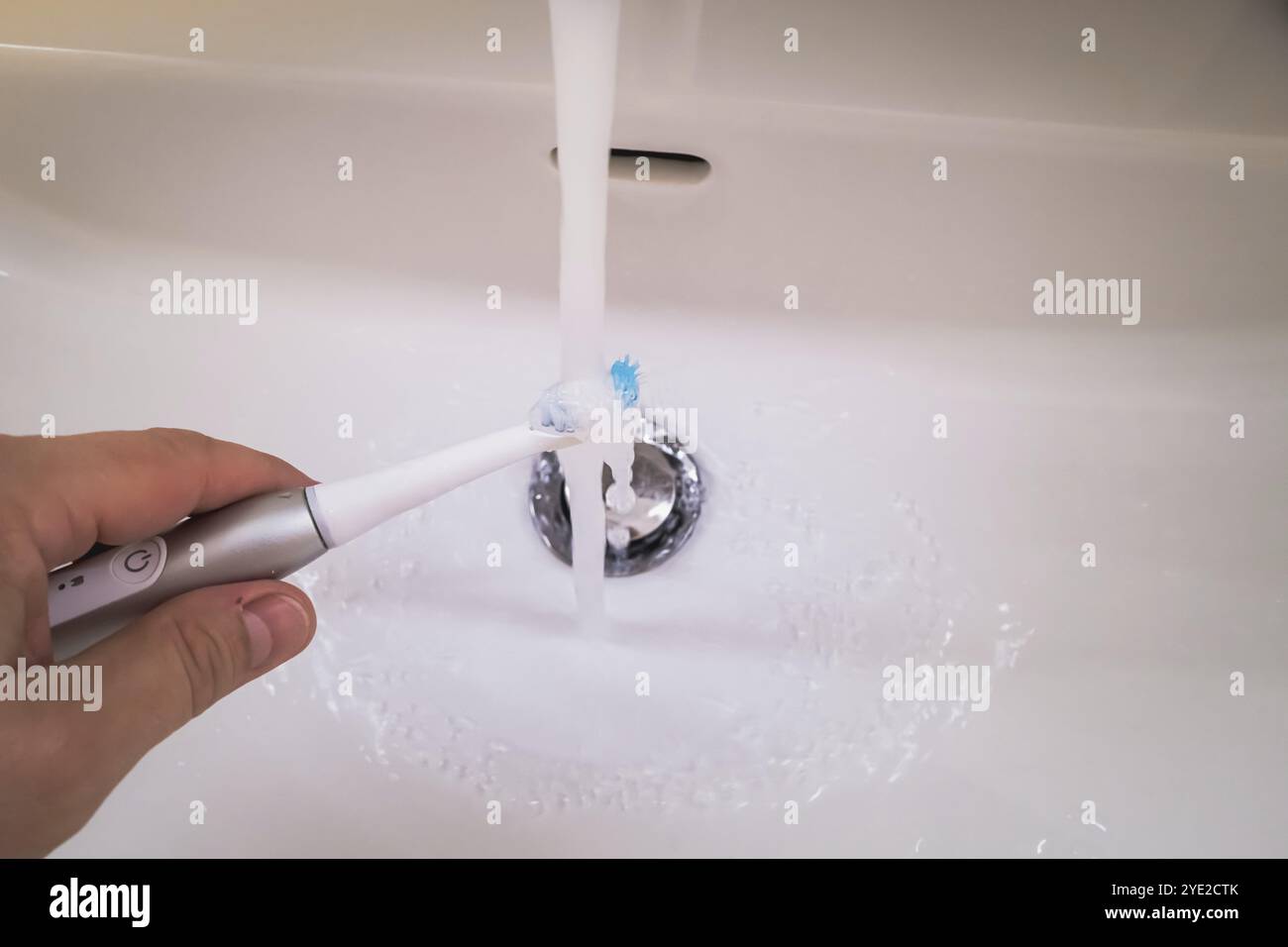 A bathroom tap is running while a toothbrush is held under the running ...