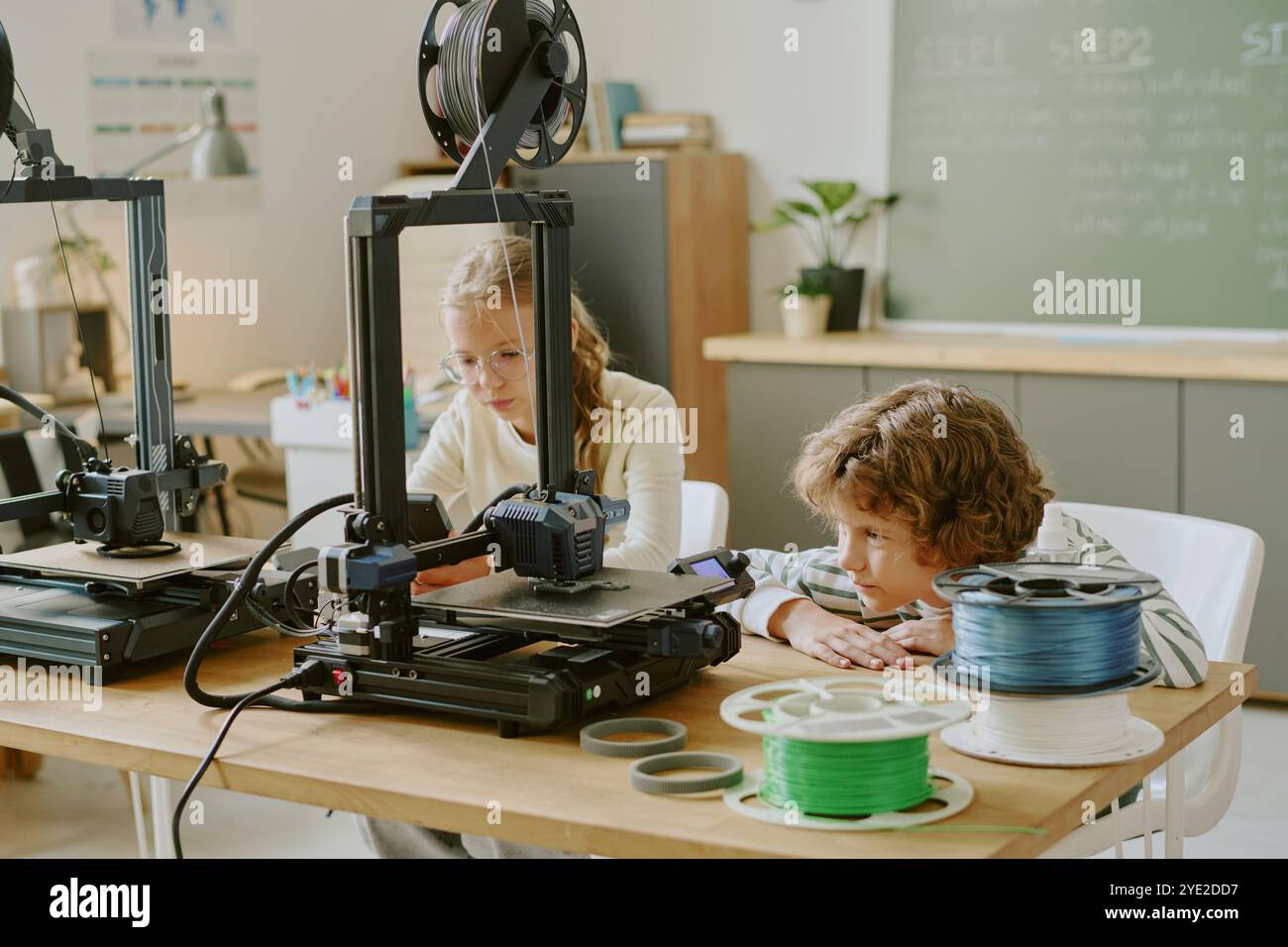 Two children working with a 3D printer in a classroom setting, engaged ...