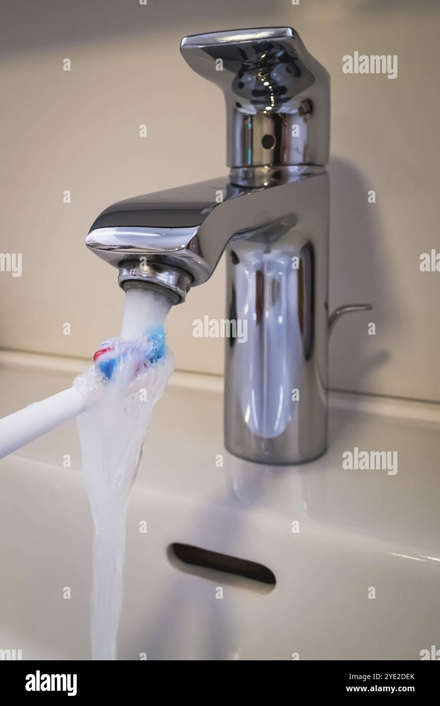A bathroom tap is running while a toothbrush is held under the running ...