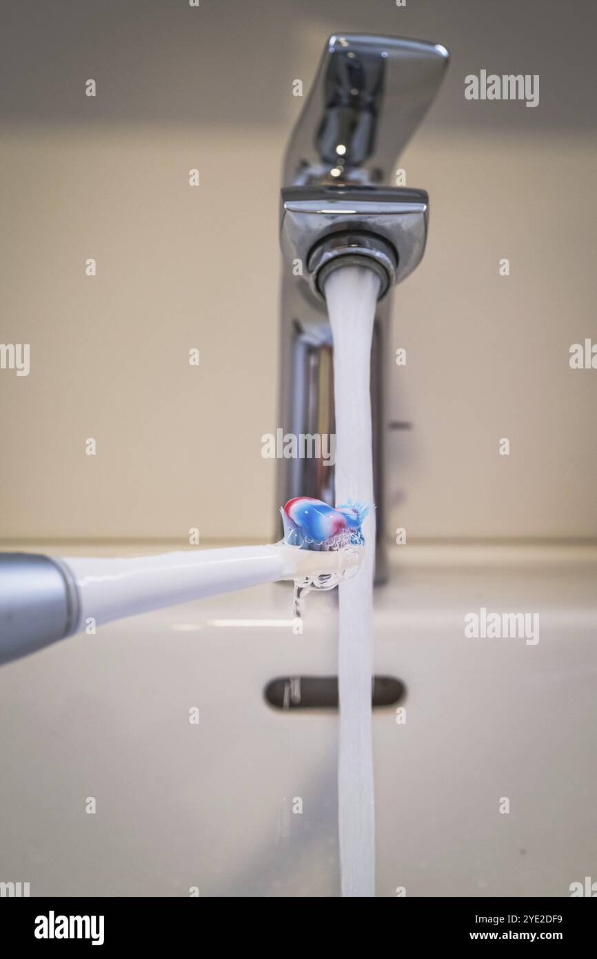 A bathroom tap is running while a toothbrush is held under the running ...