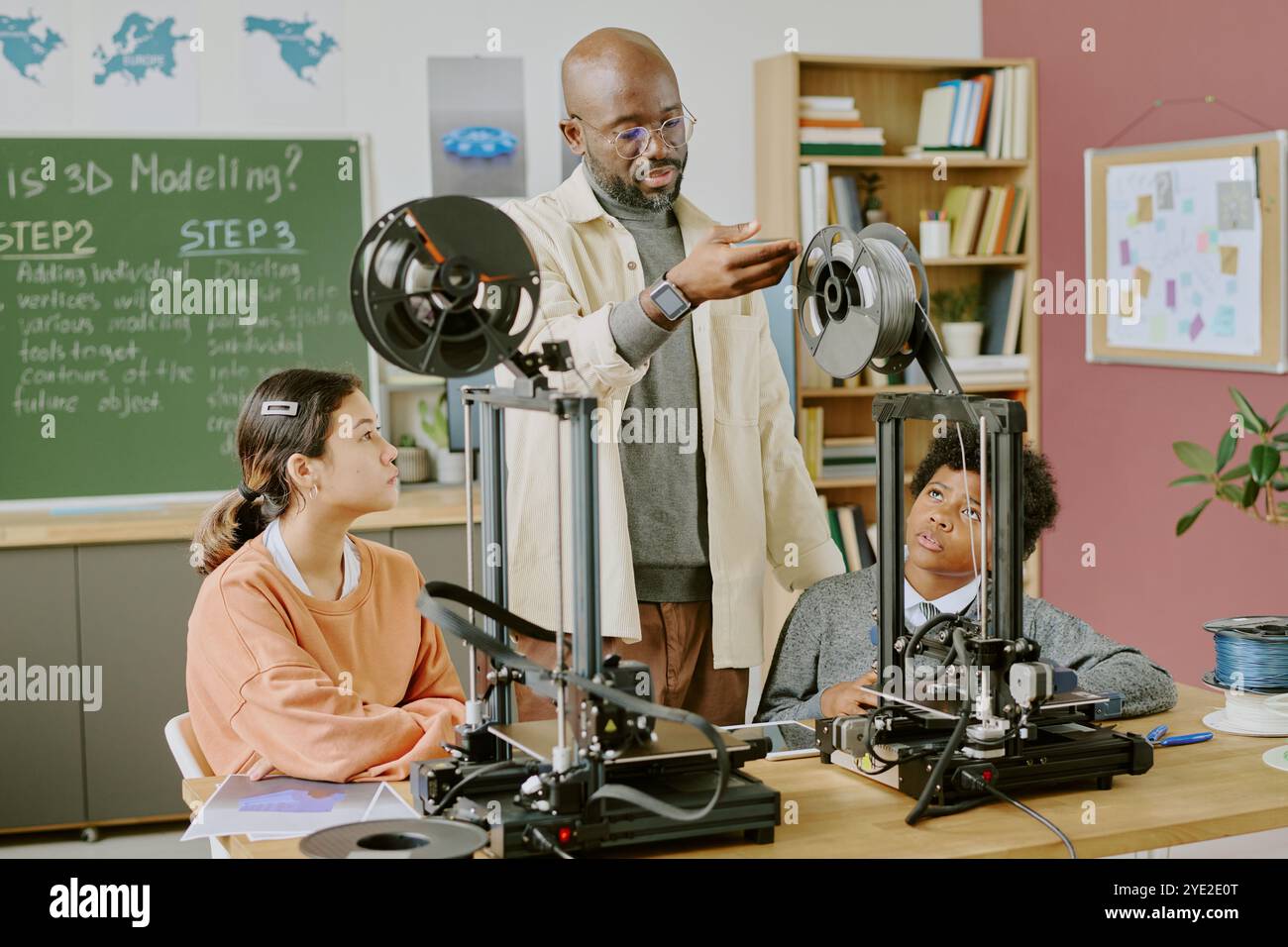 Teacher explaining 3D printing setup to attentive students in classroom ...