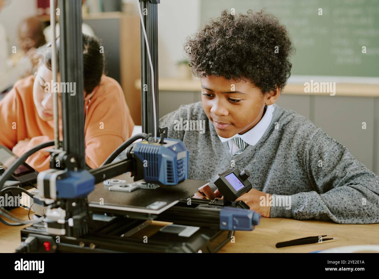 Boy working with 3D printer in classroom, carefully observing process ...