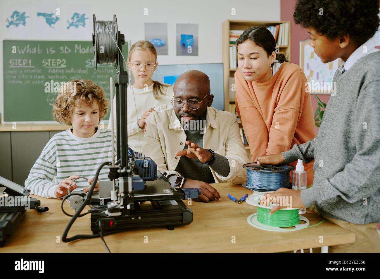 Diverse group of students gathered around a teacher explaining 3D ...