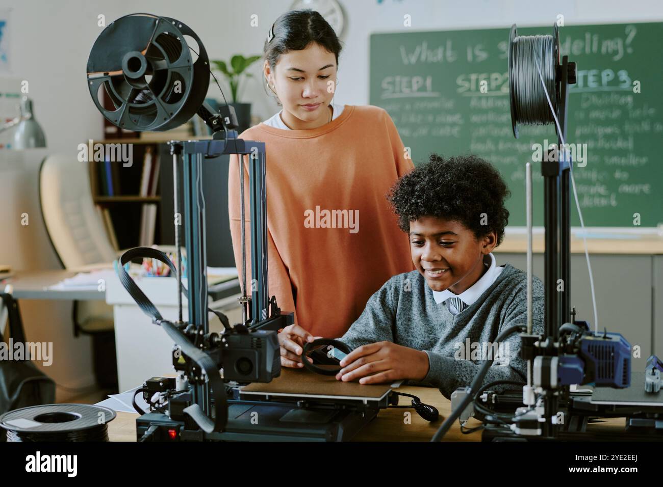 Female instructor guiding young male student in 3D printing process in ...