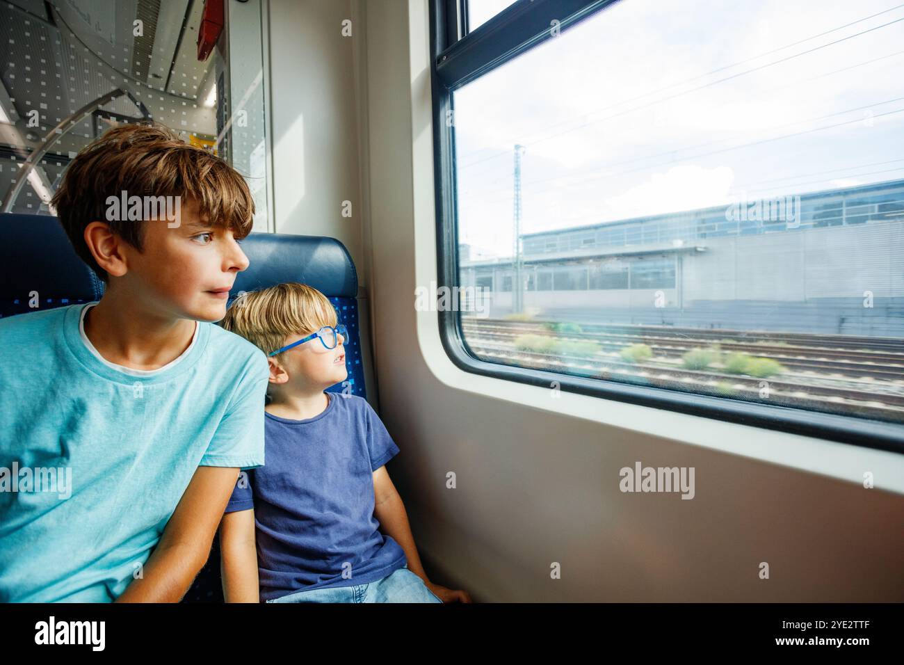 Two young boys enjoy a train ride, gaze out the window at city Stock ...