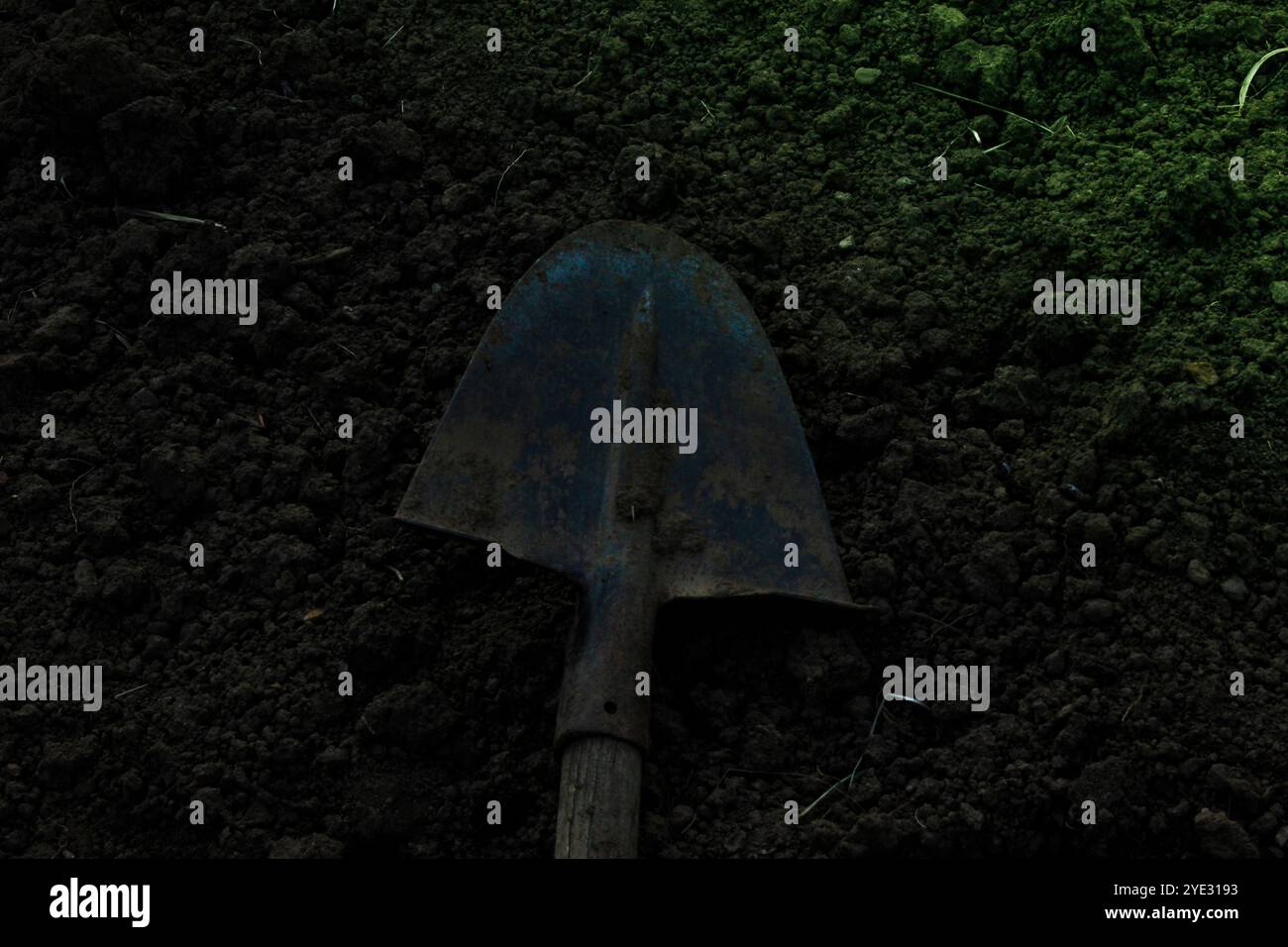 spade on barren earth photographed at night with a slight glow coming ...