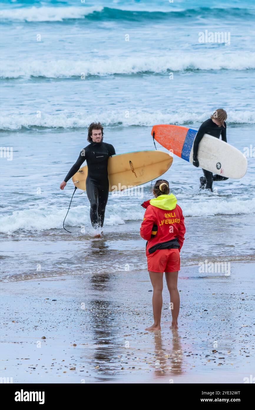 A female RNLI Lifeguard giving safety advice to surfers on Fistral ...