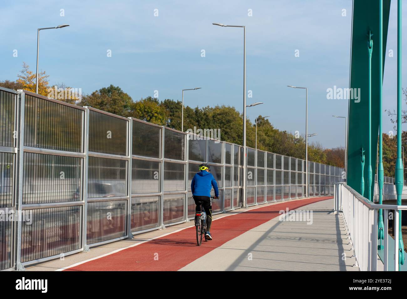 Cyclist riding on a designated bike path with safety helmet on a clear autumn day, surrounded by ...
