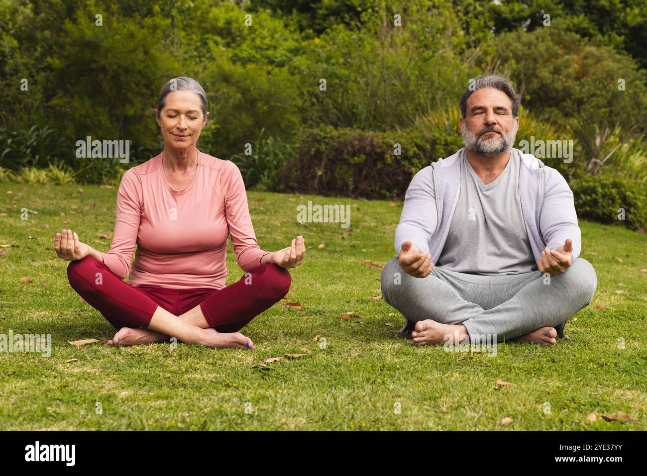 Mature couple meditating outdoors on grass, finding peace and ...