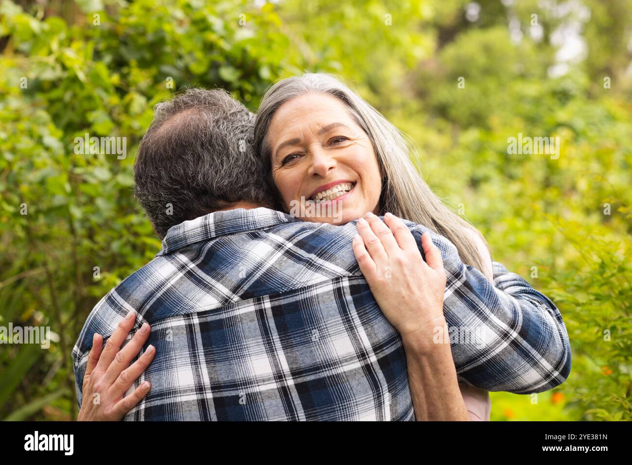 Happy mature couple embracing outdoors, woman smiling joyfully in lush ...