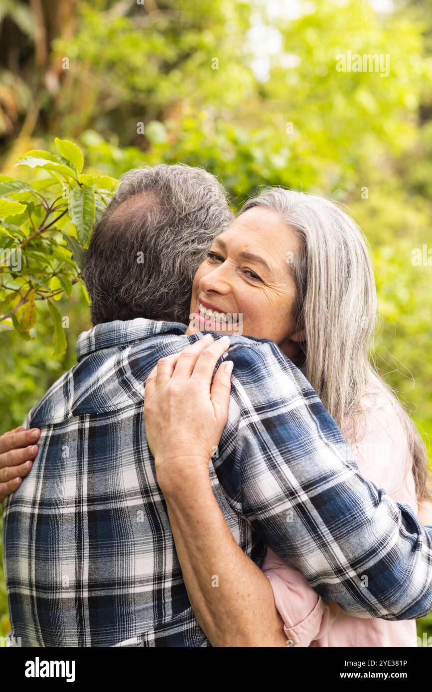 Mature couple embracing outdoors, woman smiling warmly in lush garden ...