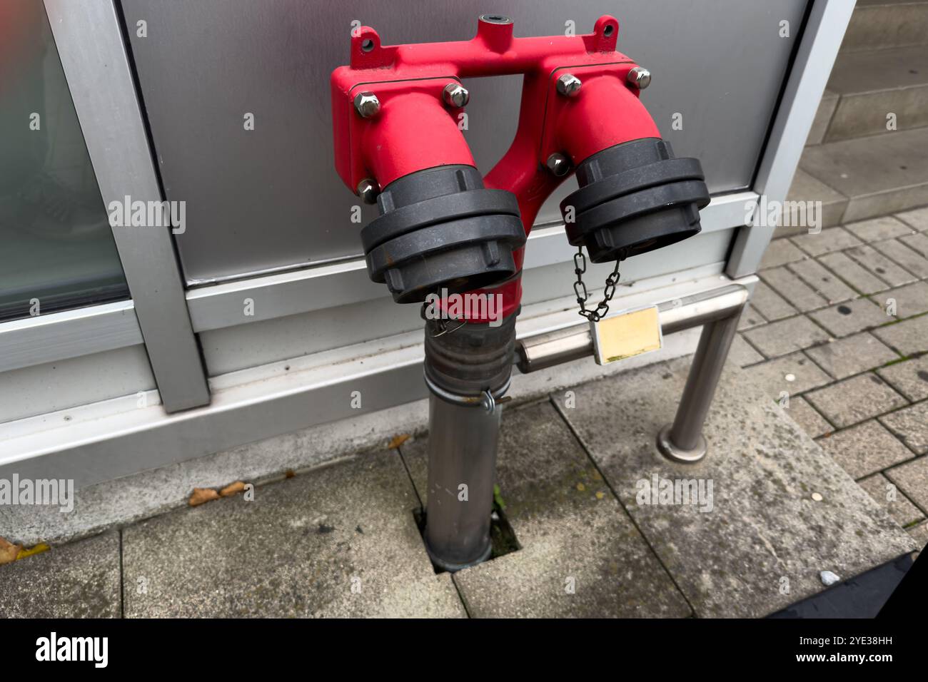 A bright red fire hydrant connection sits on the sidewalk near a ...
