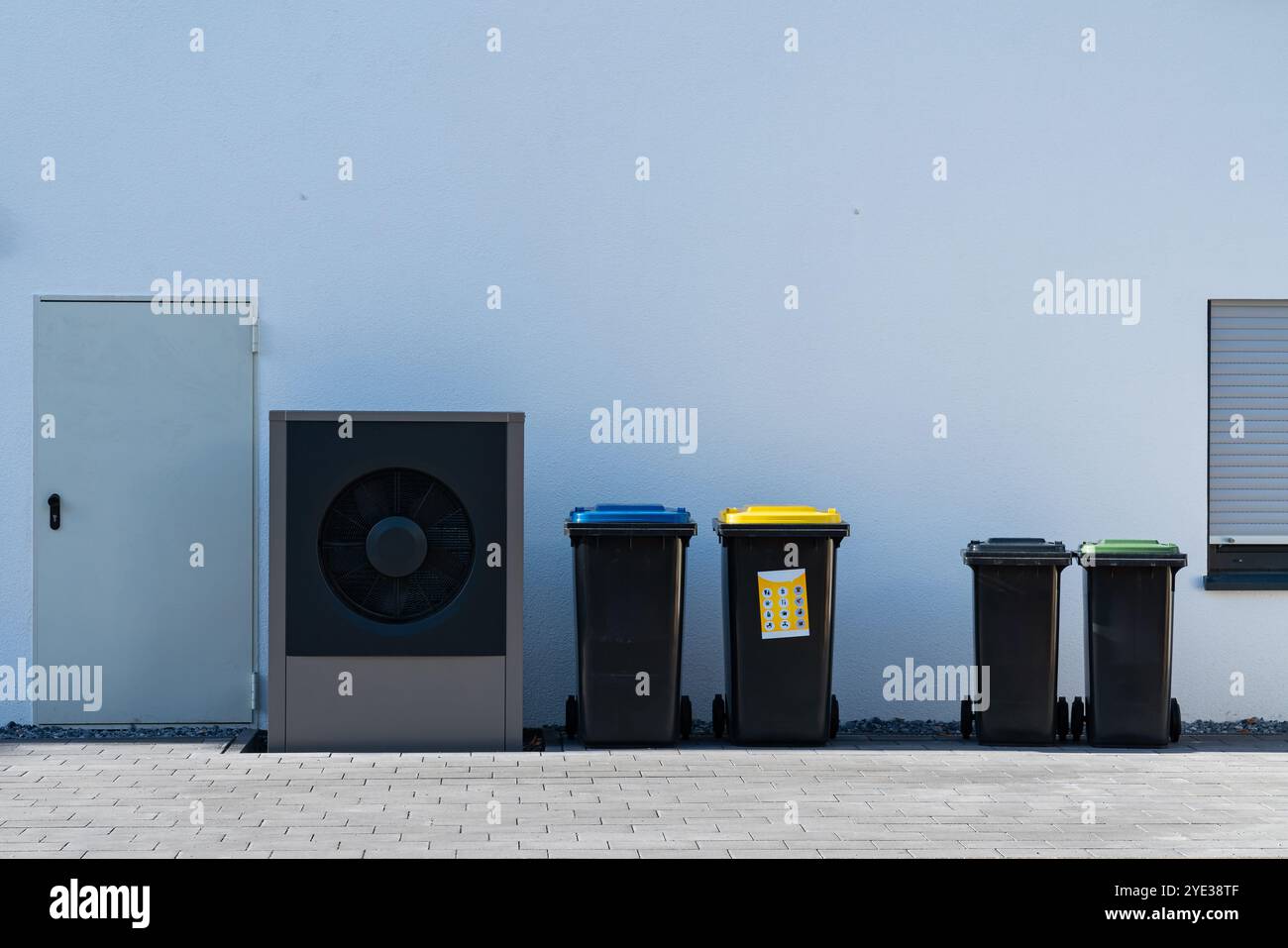 A bulk waste unit stands alongside four colorful recycling bins against a plain wall ...