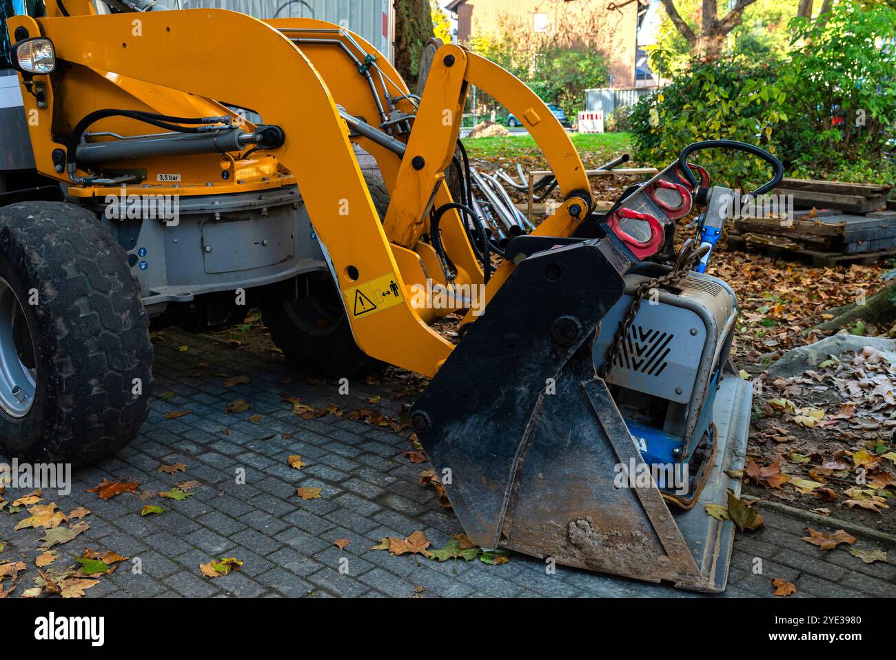 A yellow loader with a black bucket is parked on a brick driveway. The ...