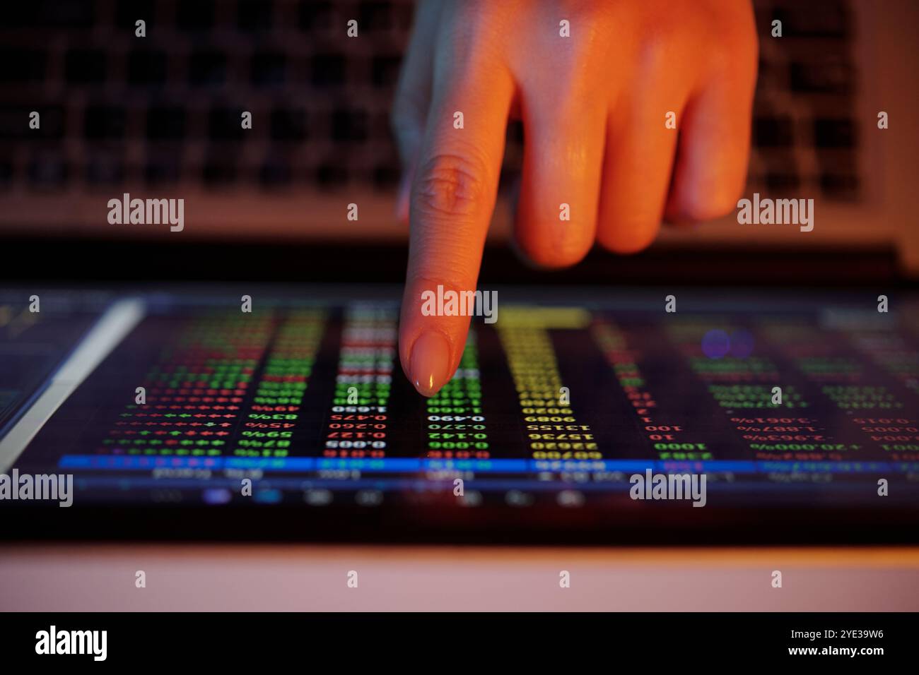 Close-up of a hand interacting with a tablet screen displaying colorful financial data charts ...