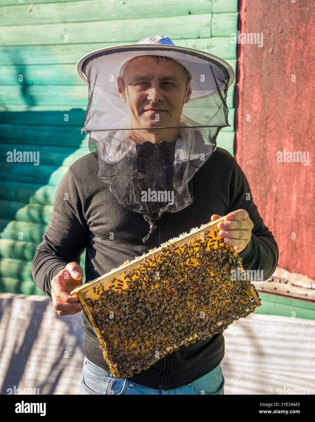 Beekeeper with protective net over his face holding honeycomb full of ...