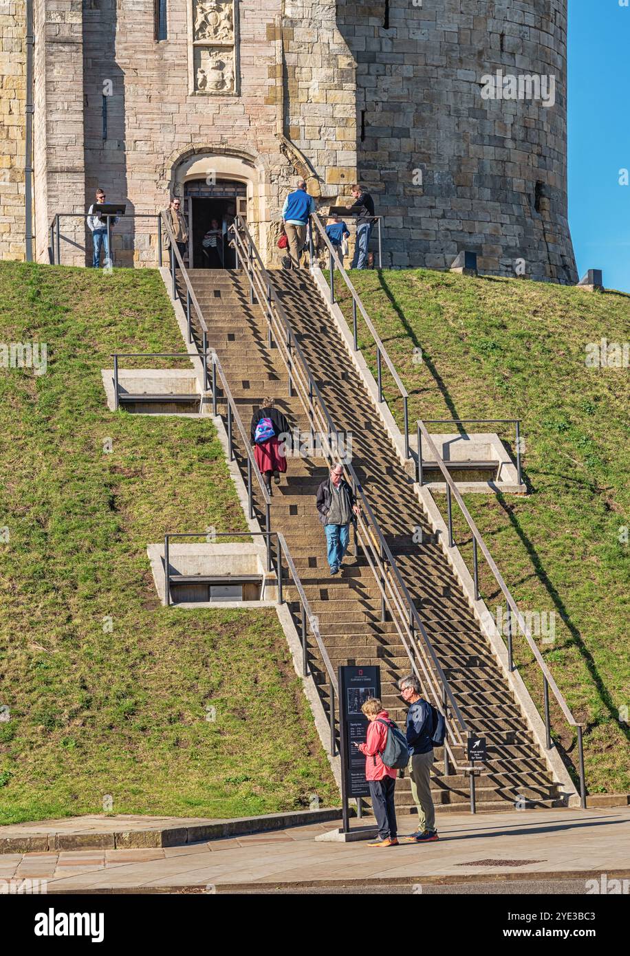 An ancient 13th Century tower on a high embankment with people milling ...