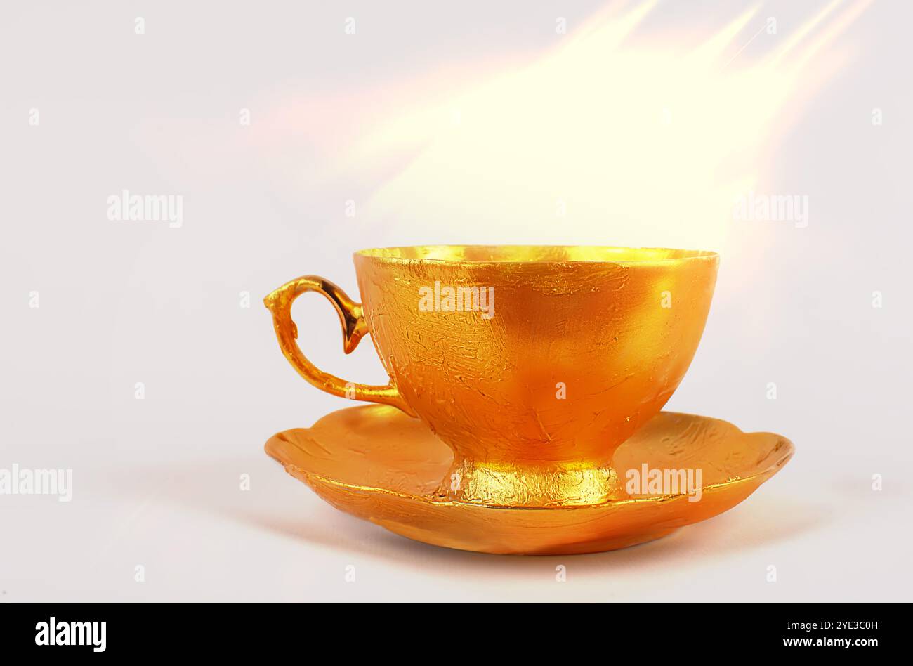 A golden tea cup with a saucer with a yellow magical glow on a pink ...