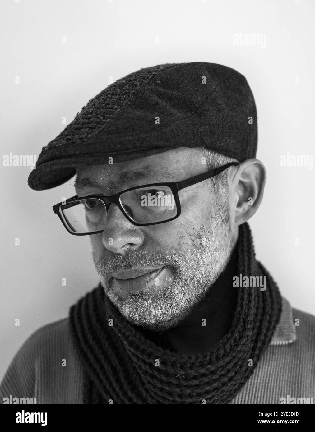 Man with cap and scarf looks down at an angle. Black and white ...