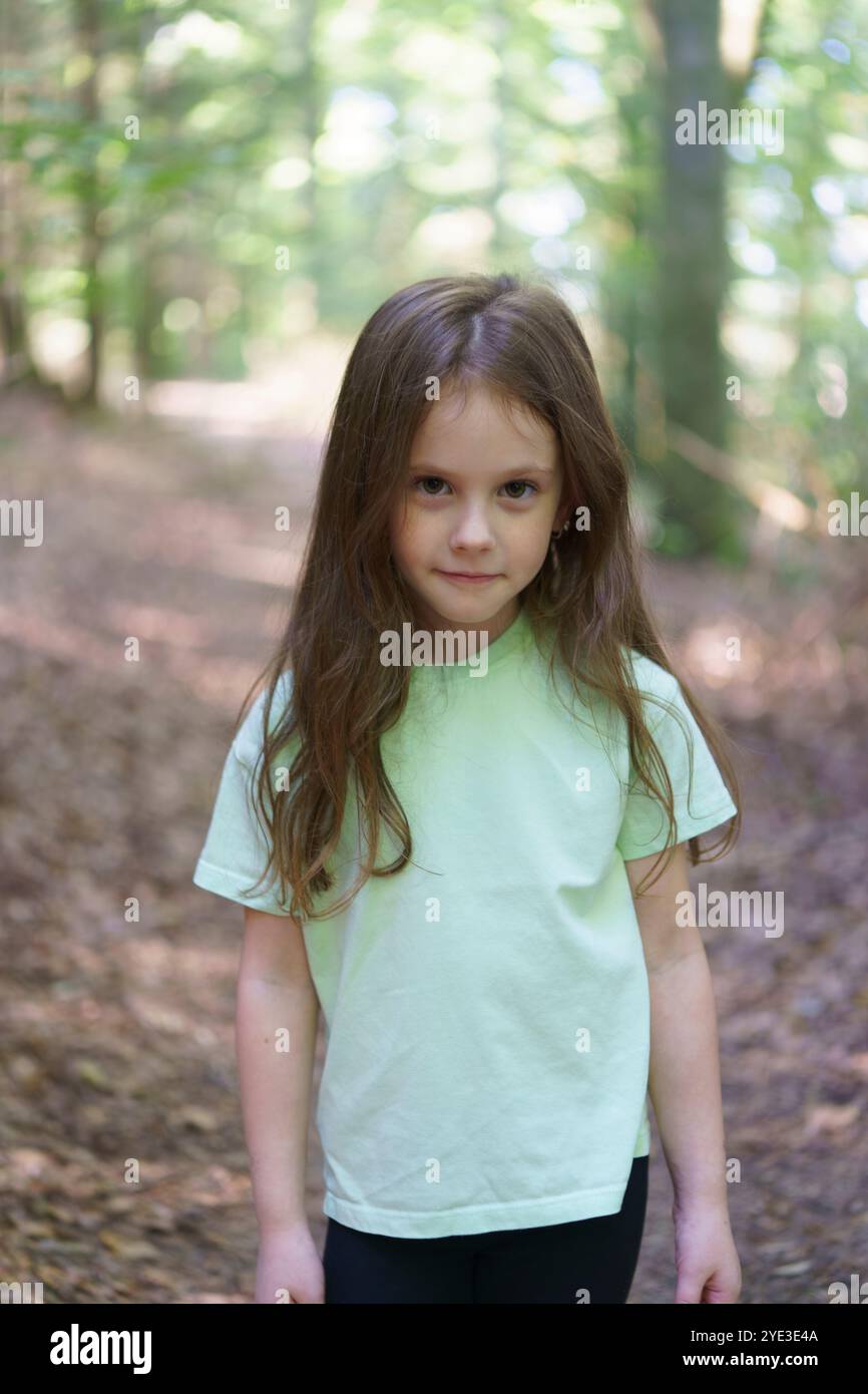 Little Girl In Green T Shirt Stands Alone In Forest Among Trees