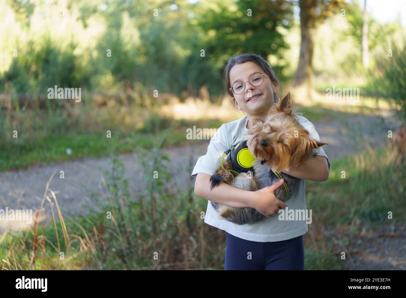 Little smiling happy girl in glasses and T-shirt stands with little ...