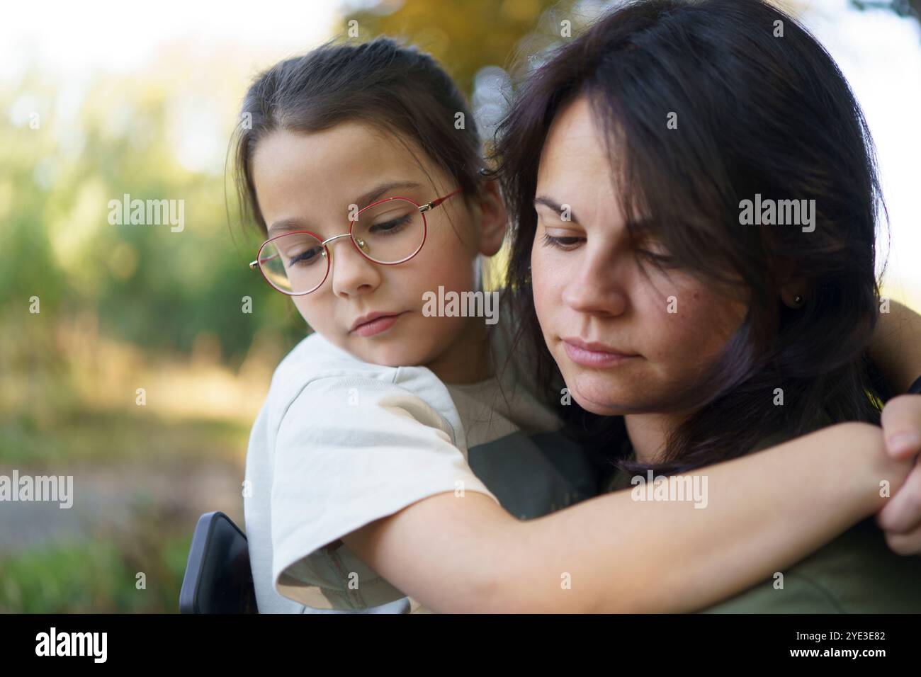 Young mother hugging her daughter while sitting on a bench in the park. Concept of happy family ...