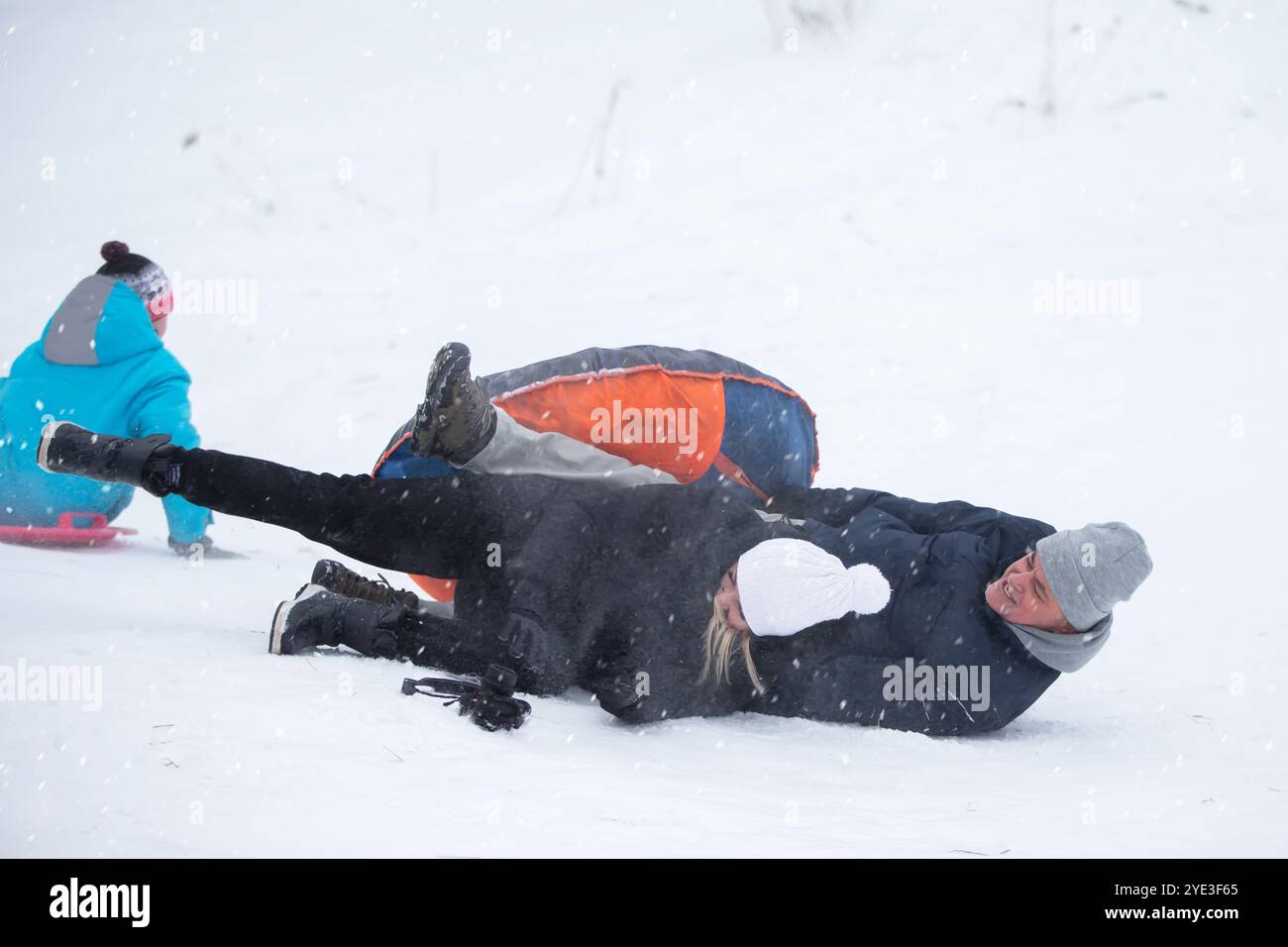 Adults fall off a snow slide while tubing Stock Photo - Alamy