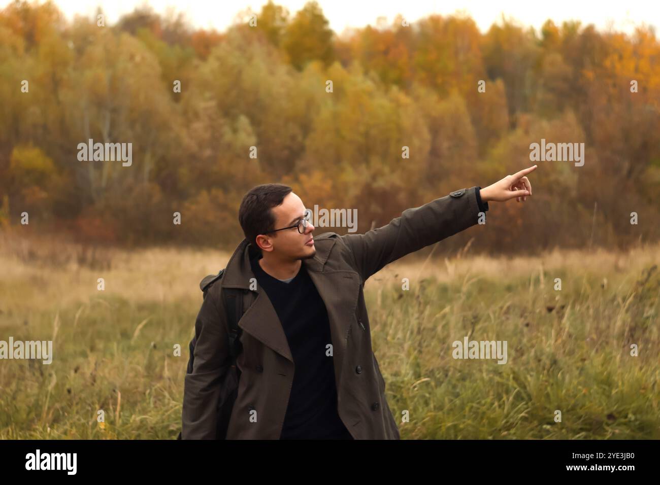 A young man in an autumn forest, pointing his finger to show direction ...