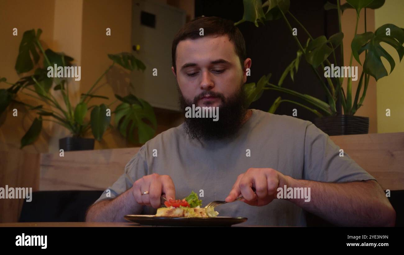 Using fork and knife utensils, a man consumes his food order. A young ...