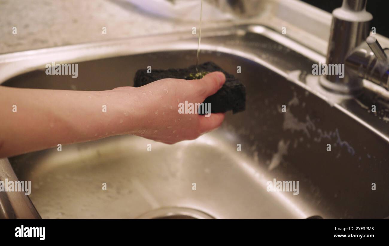 A pair of hands washes a stainless steel kitchen surface with a sponge ...