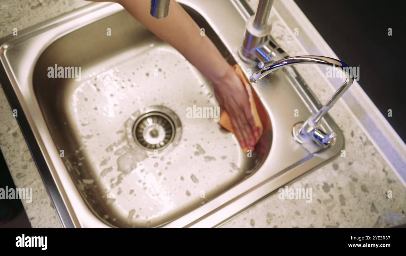 Hands wipe metal part and kitchen sink. The scene reflects the essence ...