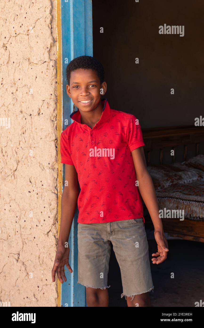 village portrait of a single african boy standing in front of the mud ...