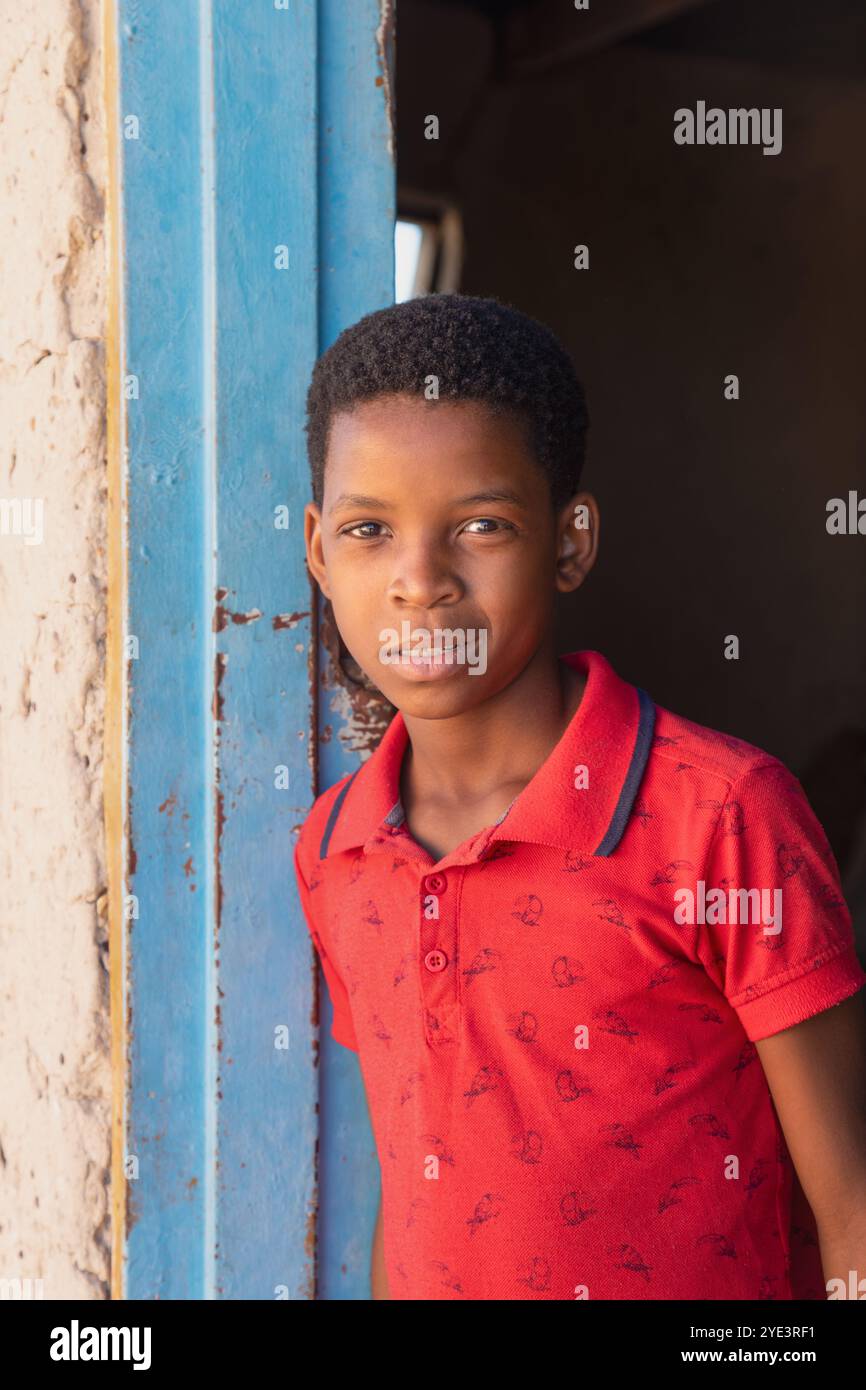 village portrait of a single african boy standing in front of the house ...