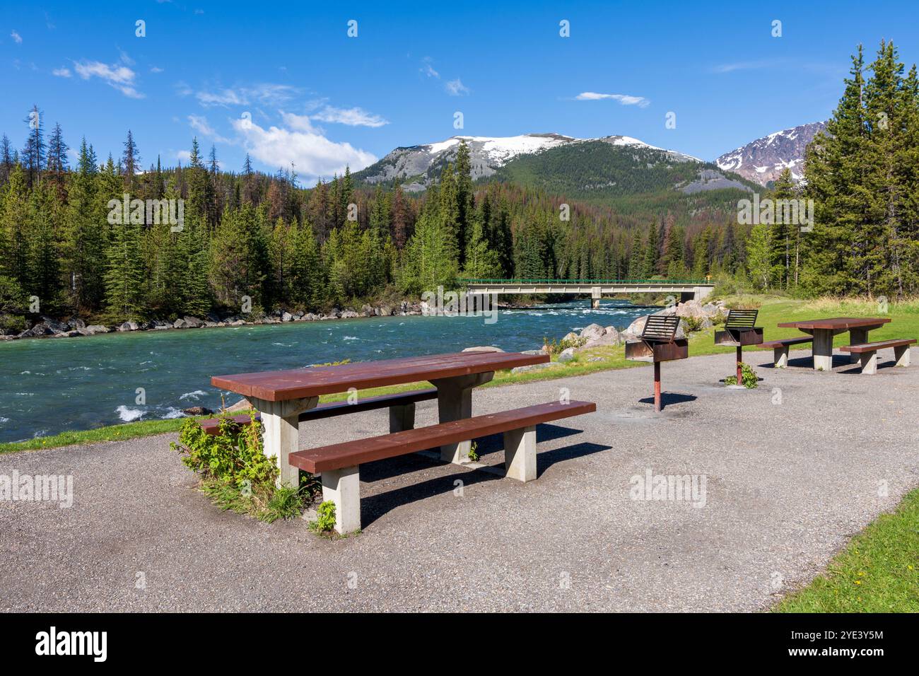 picnic table and benches on the green meadow next to a river. Mountain ...